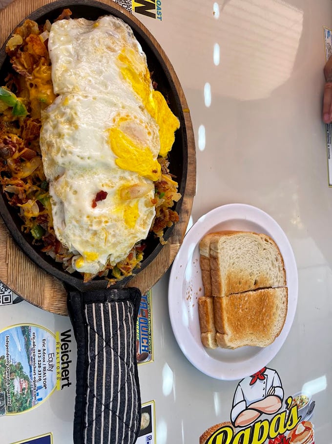 Breakfast nirvana on a sizzling skillet&mdash;eggs lounging atop a mountain of hash browns and fixings, with toast standing by for dipping duty.