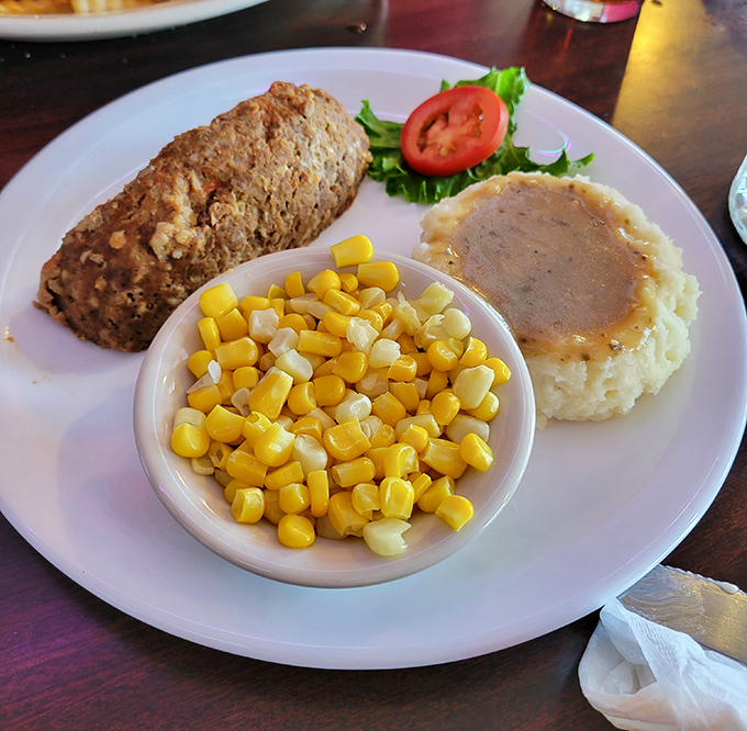 The holy trinity of comfort: meatloaf with a perfect crust, mashed potatoes with a gravy lake, and corn that pops with color. Nostalgia never tasted so satisfying.