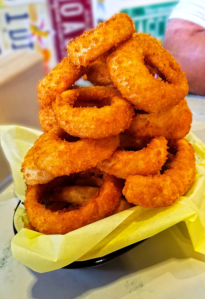 Golden onion rings stacked like edible architecture &ndash; crispy perfection that makes waiting absolutely worthwhile.