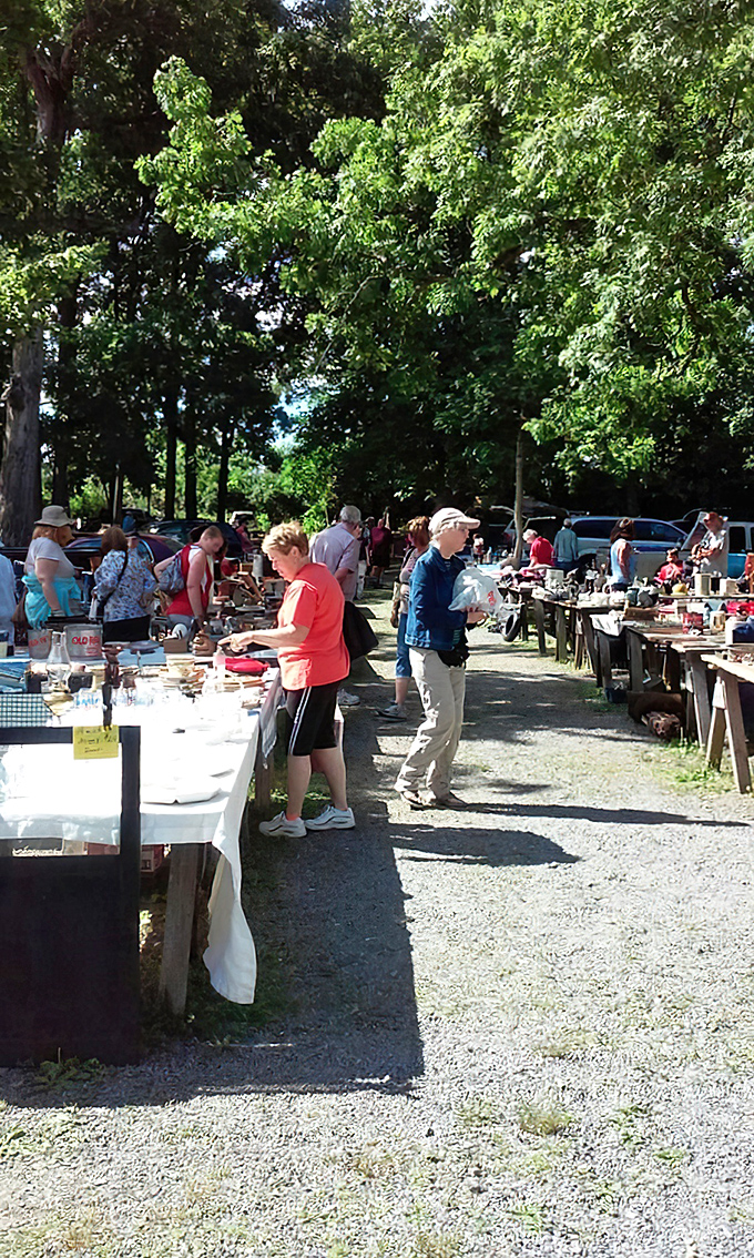 Serious collectors and curious browsers mingle beneath the leafy canopy. The dappled sunlight adds a magical quality to this outdoor treasure hunt.