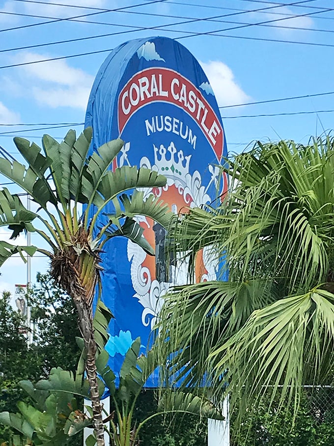 The colorful Coral Castle Museum sign stands tall among tropical palms, like a cheerful sentinel guarding Florida's most puzzling attraction.