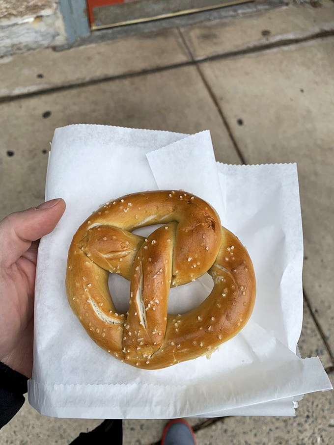 Golden, twisted perfection cradled in white paper. This isn't just a pretzel; it's edible architecture with a sprinkle of history.