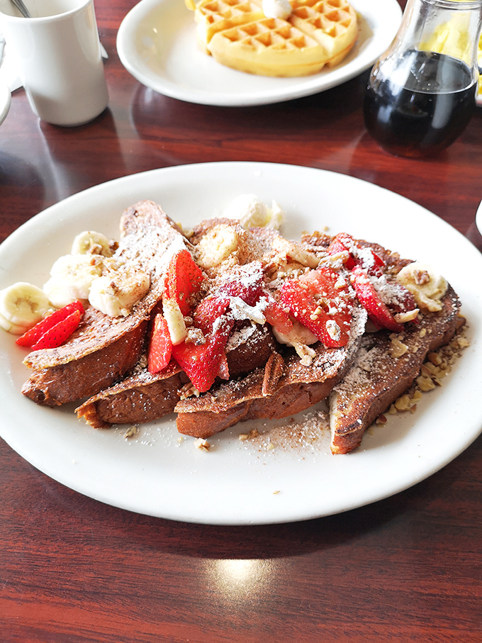 French toast nirvana! Thick-cut bread crowned with fresh strawberries, bananas, and a dusting of powdered sugar that whispers, "Take the day off."
