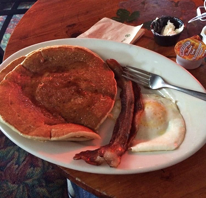 The red-hued glow adds a touch of dive bar magic to this classic breakfast plate &ndash; pancakes, crispy bacon, and eggs cooked just right.