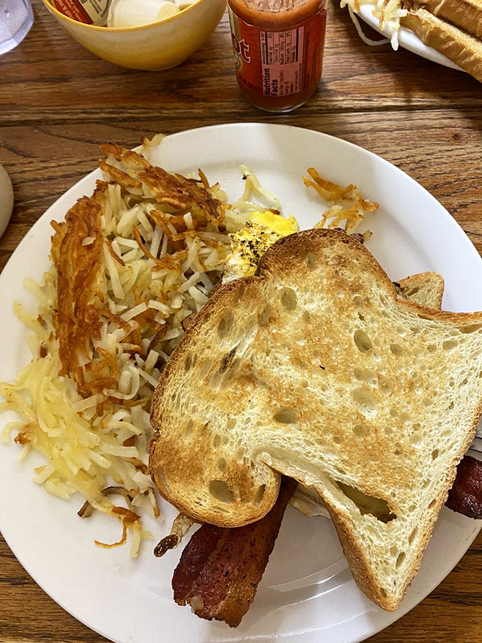 The breakfast trinity: perfectly crispy hash browns, golden toast, and bacon that would make even vegetarians reconsider their life choices.