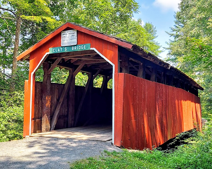 Clay's Bridge stands as a crimson sentinel of bygone days, its weathered boards whispering stories of horse-drawn carriages and simpler times.