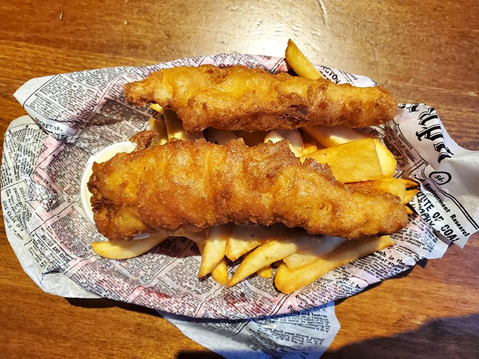Two perfectly fried cod fillets lounging on a bed of chips, wrapped in faux newspaper. The British tabloids never tasted this good.