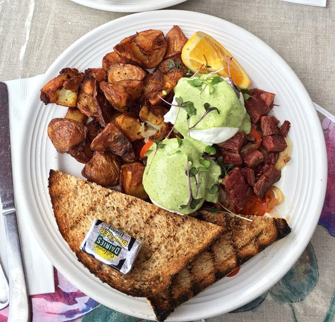 Golden-brown potatoes surround poached eggs wearing a jaunty green hollandaise hat &ndash; proof that breakfast can be both art and sustenance.