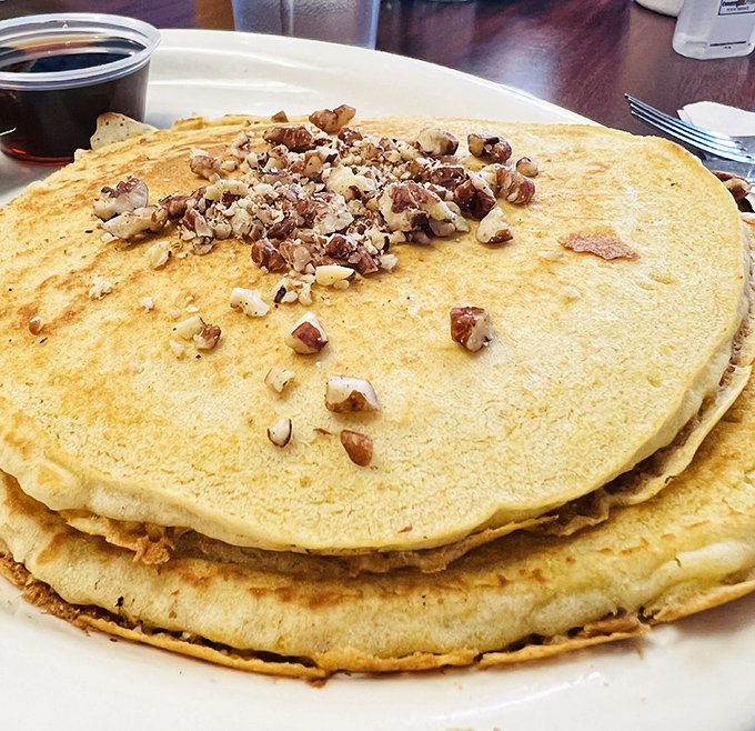 These pecan-studded pancakes aren't just breakfast, they're an argument against every other food group. The maple syrup cup stands by, ready for its supporting role.