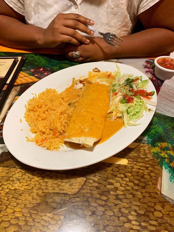 The burrito arrives like a gift wrapped in a tortilla blanket, smothered in cheese sauce that's practically begging to be photographed before it's devoured.