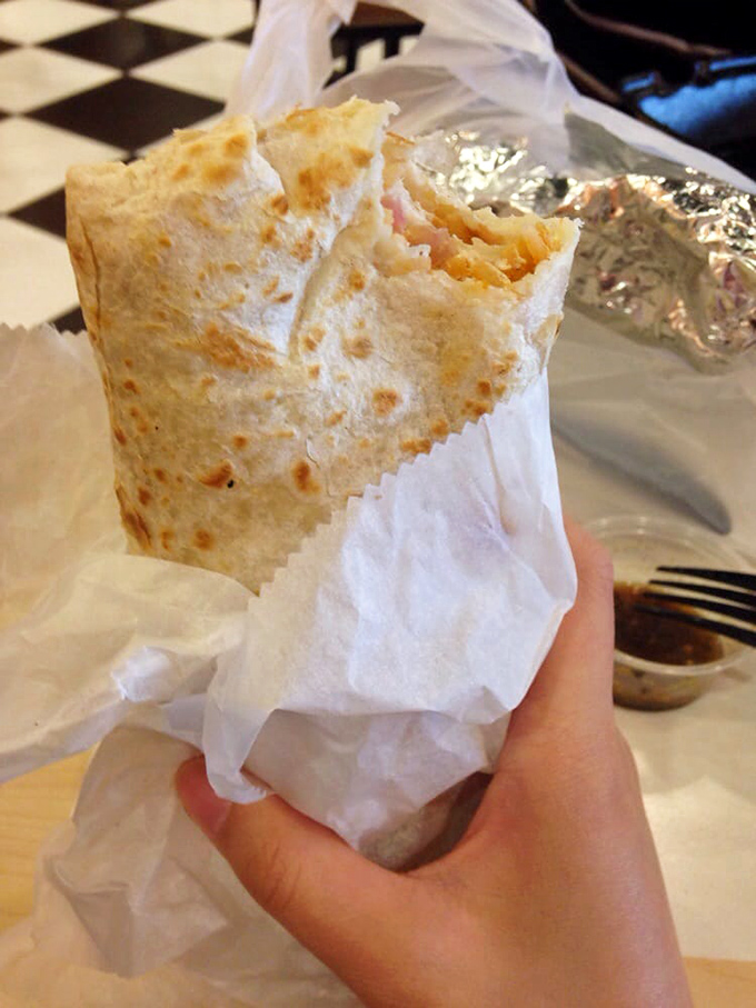That moment when paper-wrapped perfection meets eager hands. The slight char marks on the tortilla promise the ideal textural contrast within.