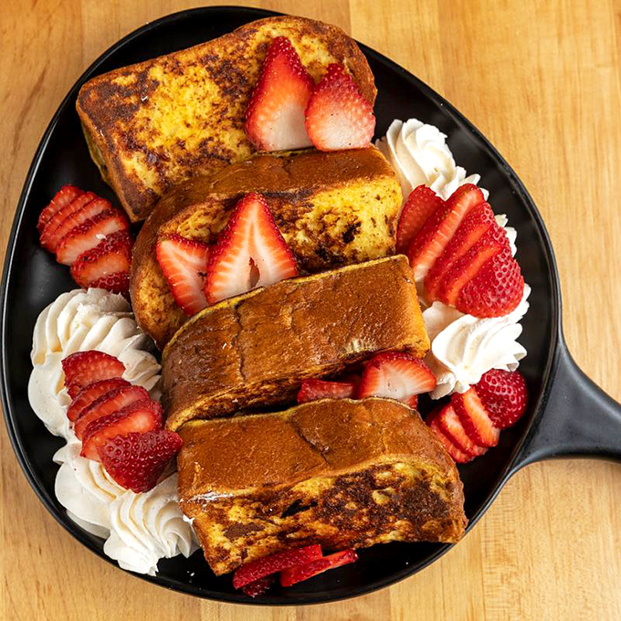 French toast that's dressed for success with strawberries, whipped cream, and enough powdered sugar to make your dentist buy a vacation home.