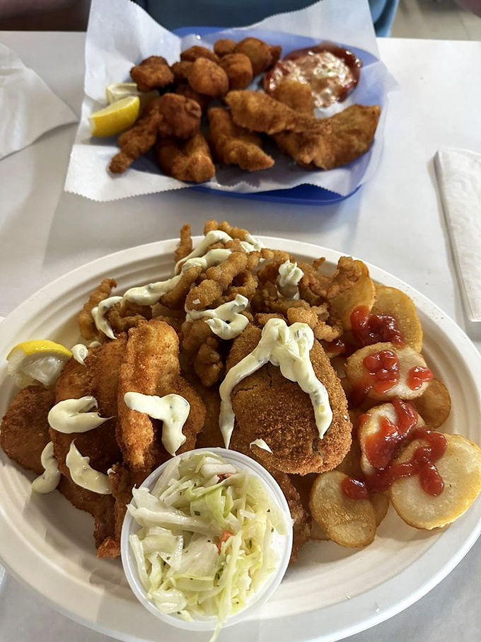 Seafood nirvana on a plate! Golden-fried treasures drizzled with tartar sauce, surrounded by crispy chips and that essential lemon wedge standing by for duty.