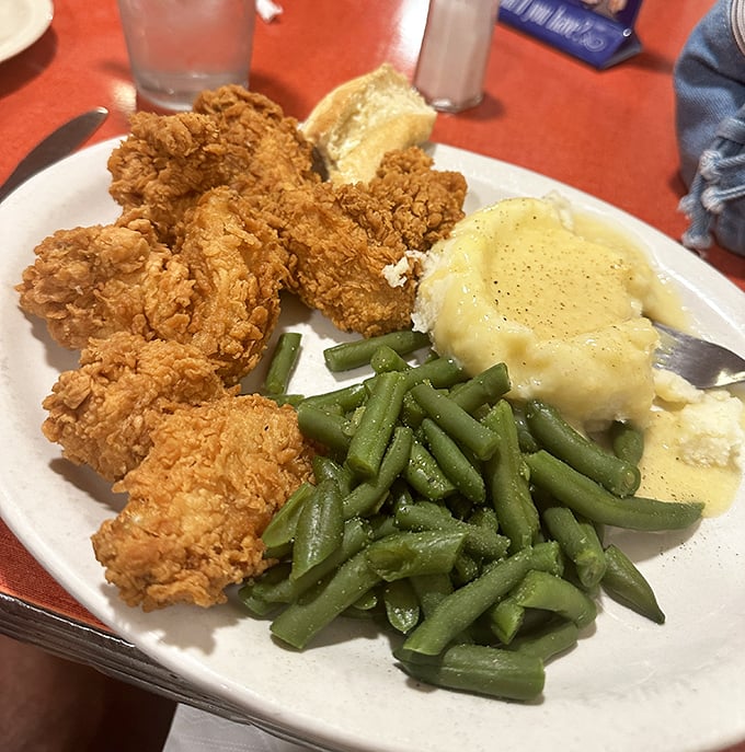 The holy trinity of comfort: perfectly fried chicken, vibrant green beans, and mashed potatoes swimming in gravy that should be declared a national treasure.