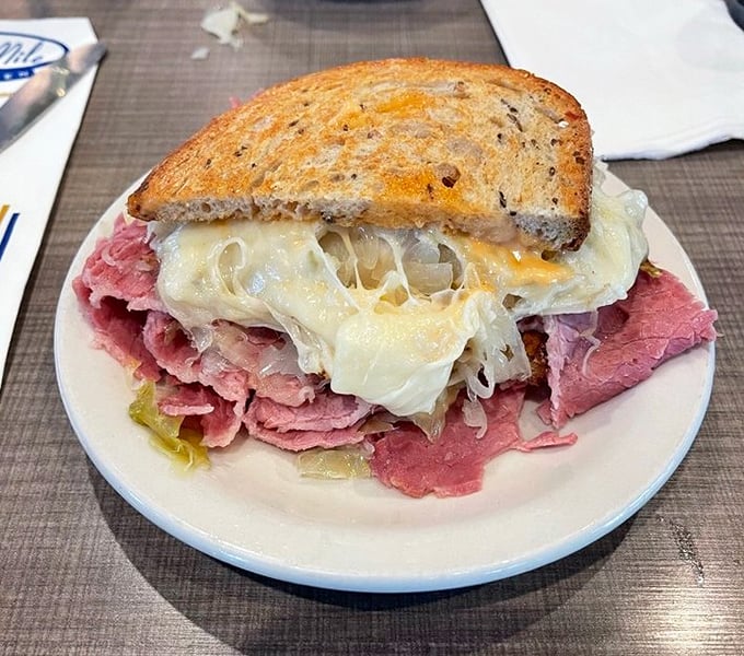 The half Reuben reveals its secrets &ndash; layers of tender corned beef, tangy sauerkraut, and melted Swiss cheese creating the holy trinity of sandwich perfection.