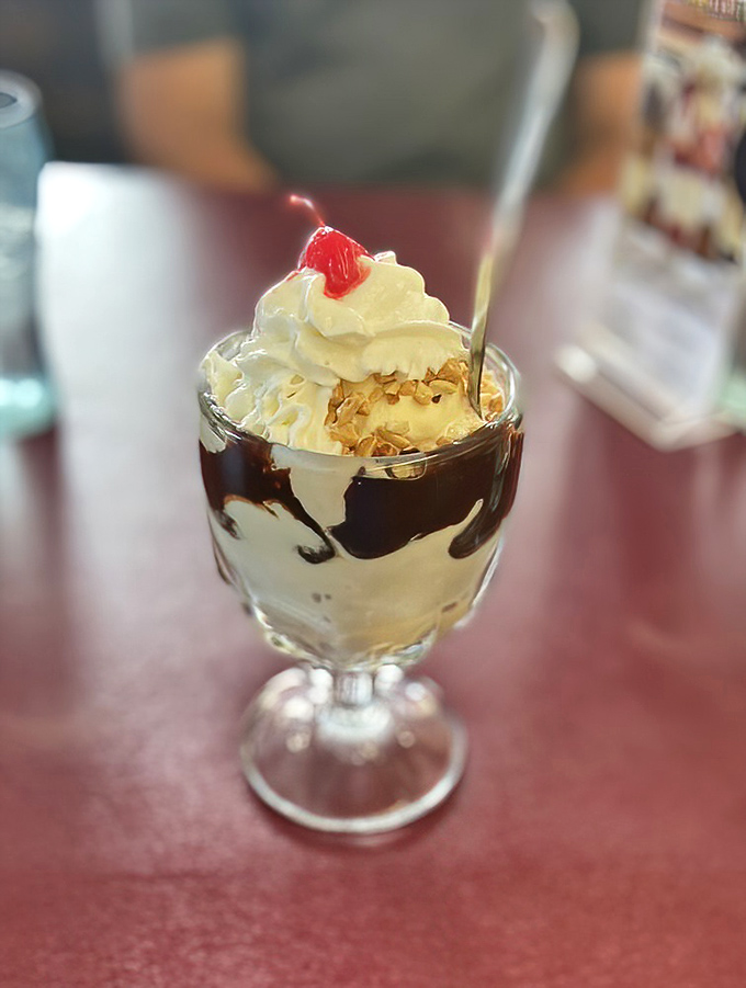 Hot fudge cascades over vanilla ice cream like chocolate lava, topped with a cloud of whipped cream and that essential cherry beacon.