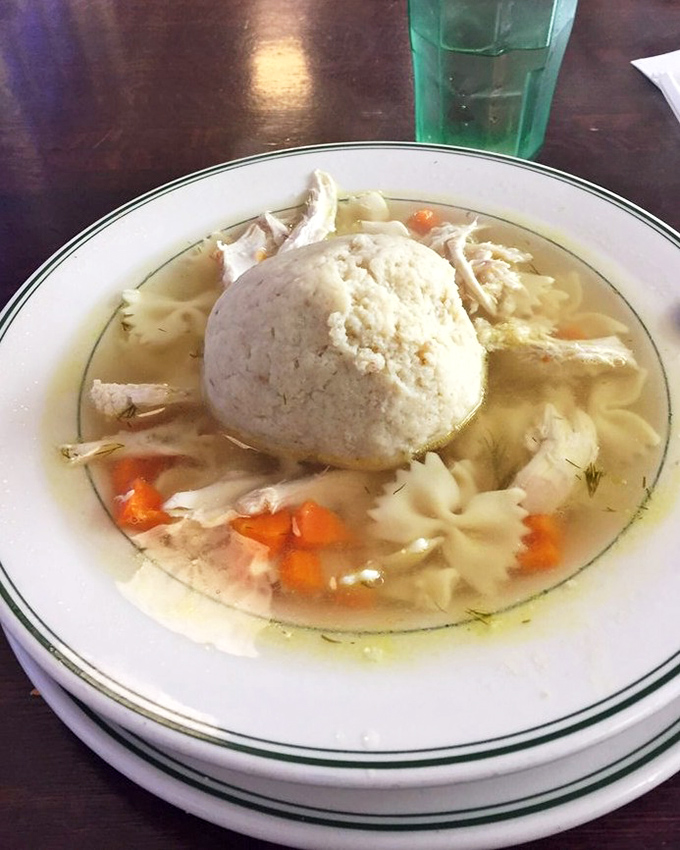 A matzo ball that could moonlight as a planet, floating in a broth so clear and golden it deserves its own display case.