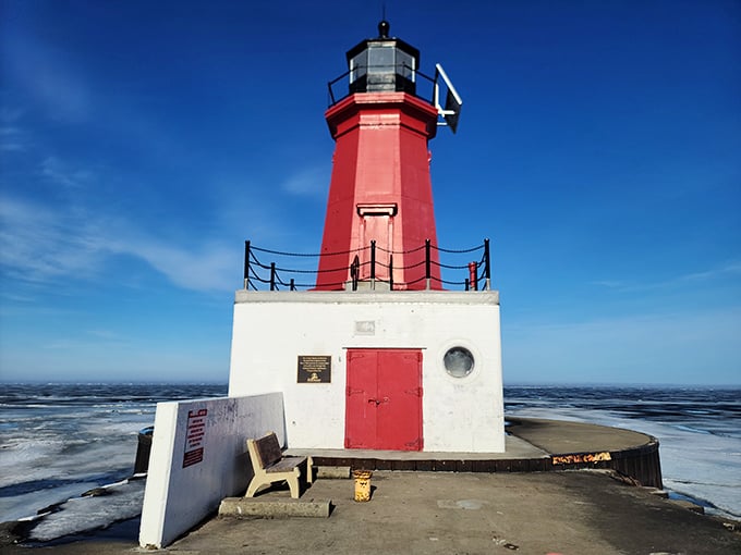 The North Pier Lighthouse stands bright against winter's grip, a flame-colored sentinel guarding Great Lakes mariners for generations.