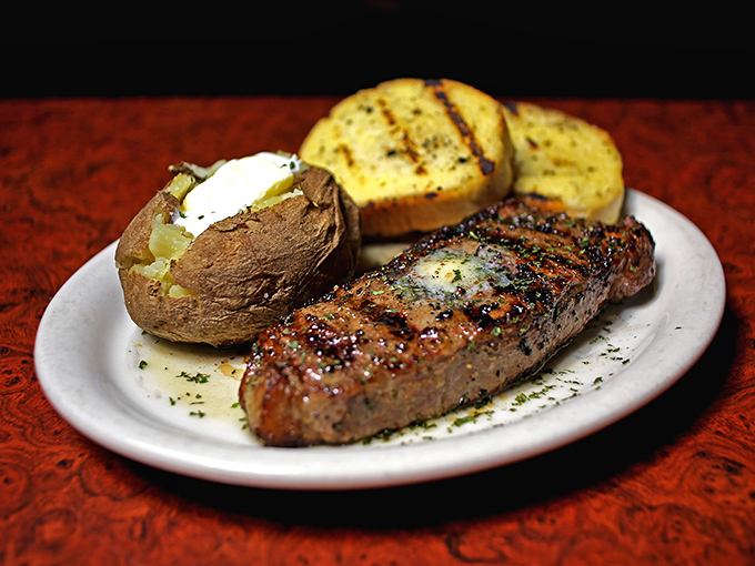 The New York Strip arrives like a work of art, resting beside a butter-laden baked potato and garlic bread&mdash;a holy trinity of steakhouse perfection.