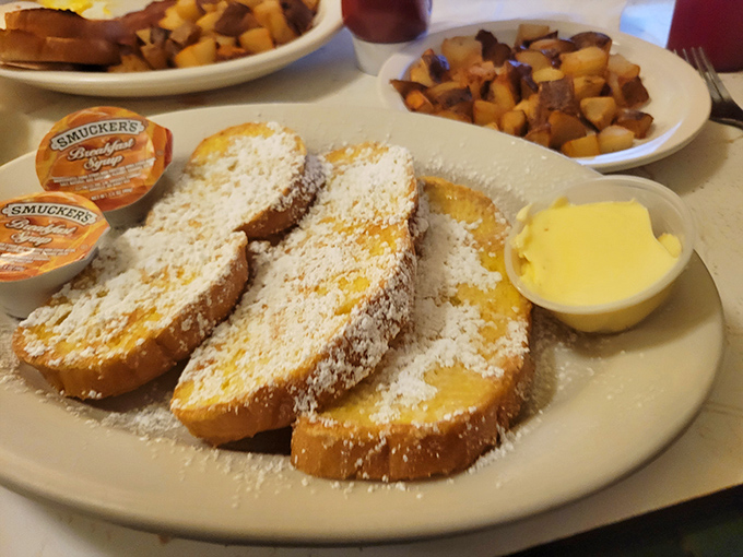 The French toast arrives dusted with powdered sugar like fresh snow, with butter melting into golden valleys and Smucker's jam standing by for the finishing touch.
