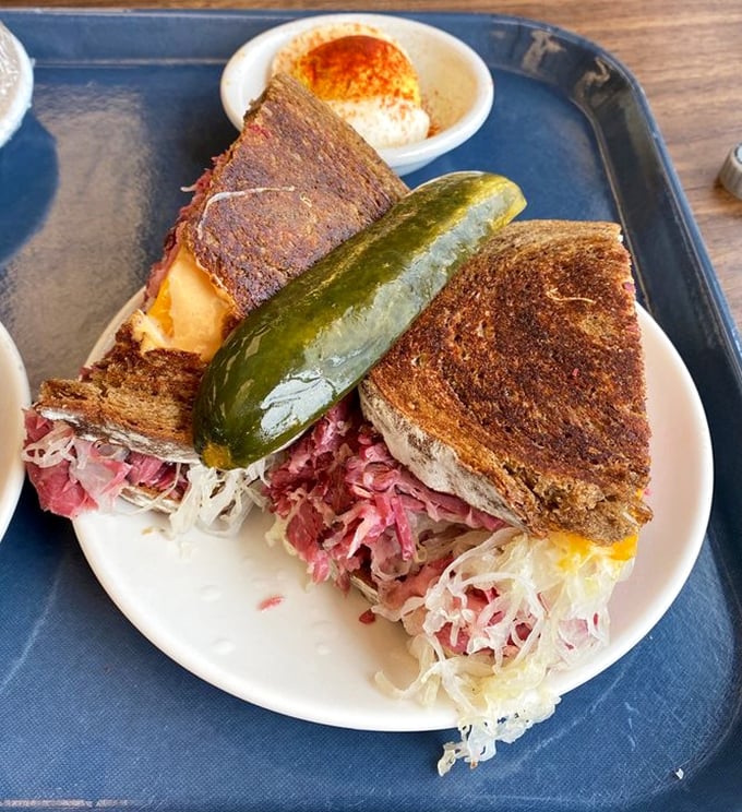 The Reuben's spicier cousin arrives with a pickle sentinel standing guard. Your diet plan just called to wave the white flag.