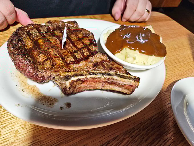 The bone-in ribeye arrives like a carnivore's dream, accompanied by mashed potatoes swimming in gravy that demands to be sopped up.