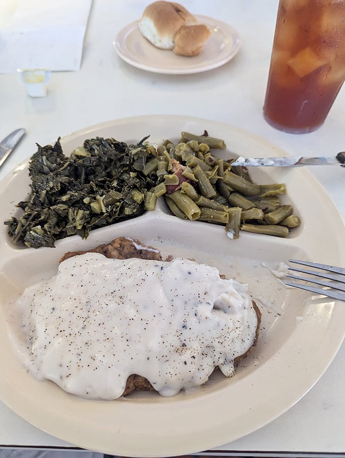 The star attraction: chicken fried steak smothered in pepper-flecked gravy alongside Southern-style green beans and collard greens. A trinity of comfort!