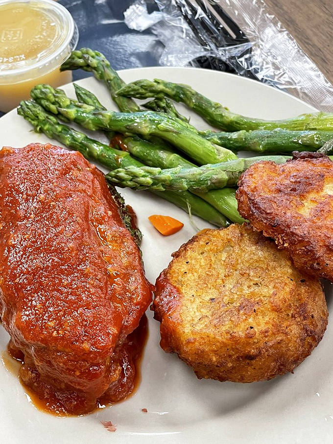 The meatloaf's tomato-glazed crown jewel sits alongside perfectly roasted potato pancakes and fresh asparagus&mdash;proof that simple food done right is culinary royalty.
