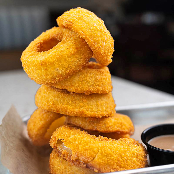 Onion rings stacked higher than my college textbooks ever were. Crispy, golden armor protecting sweet onion treasure within.