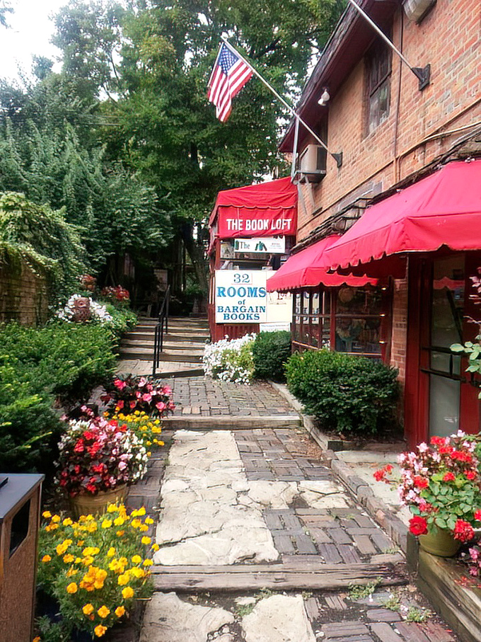 A garden path lined with flowers leads to literary treasures. The "Willkommen" sign honors German Village heritage while welcoming book lovers of all backgrounds.