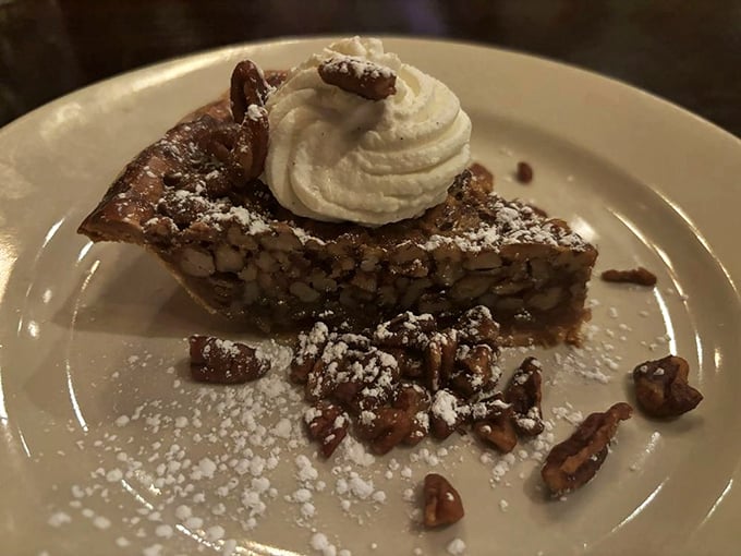 A slice of pecan pie that could make a Southerner weep with joy, topped with a cloud of whipped cream and a sprinkle of powdered sugar dreams.