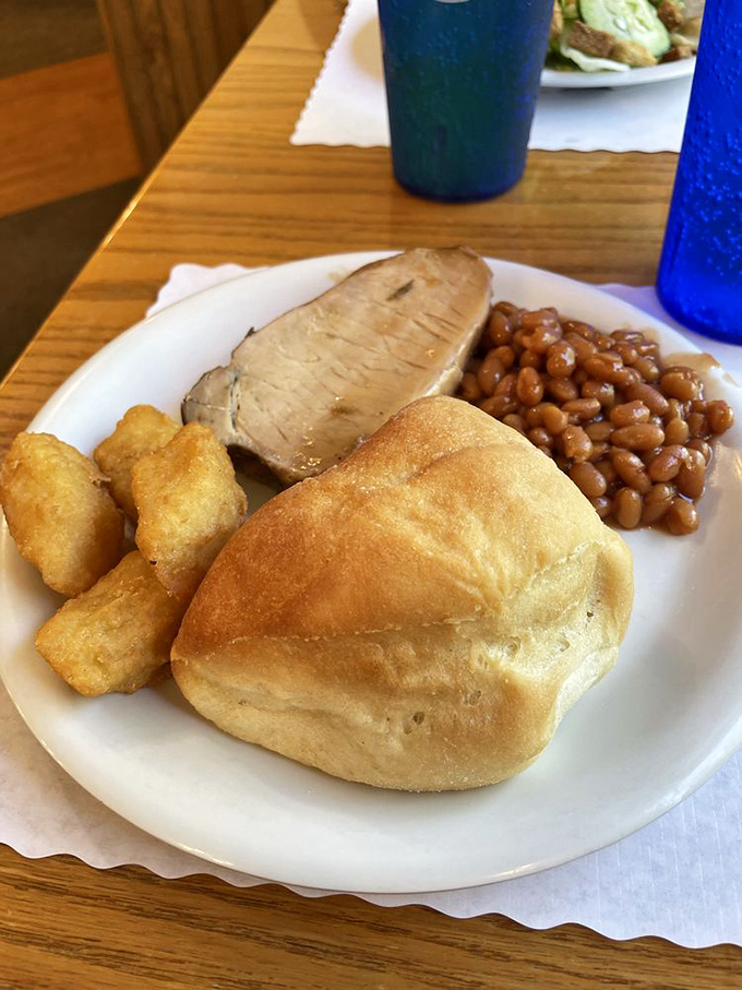 A perfect plate of Midwestern harmony &ndash; tender pork, golden tater tots, baked beans, and that dinner roll waiting to sop up every last bit of goodness.