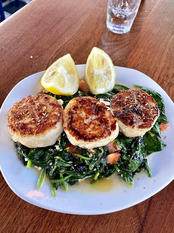 Perfectly seared scallops lounging on a bed of saut&eacute;ed greens. A trio of ocean sweetness with lemon wedges standing by for duty.