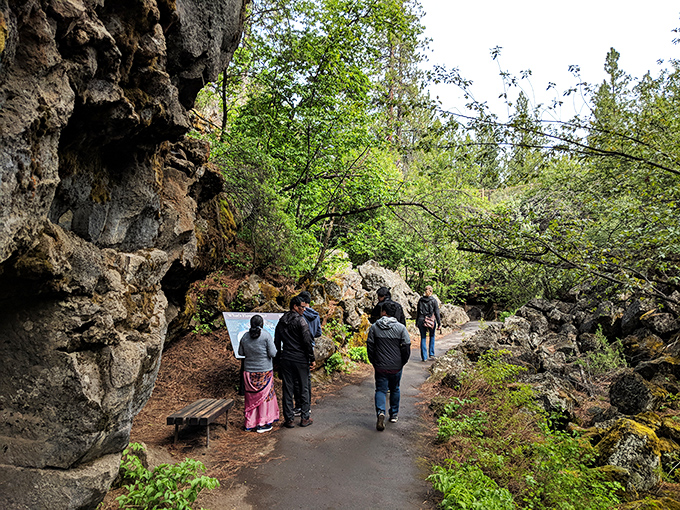Explorers gather at the cave entrance, preparing for their subterranean journey. The contrast between sunlit forest and mysterious cave opening creates an irresistible invitation to adventure.