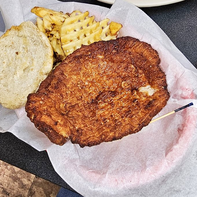 The breaded tenderloin—Indiana's unofficial state sandwich—spilling gloriously over its bun. Midwestern portion control at its finest.