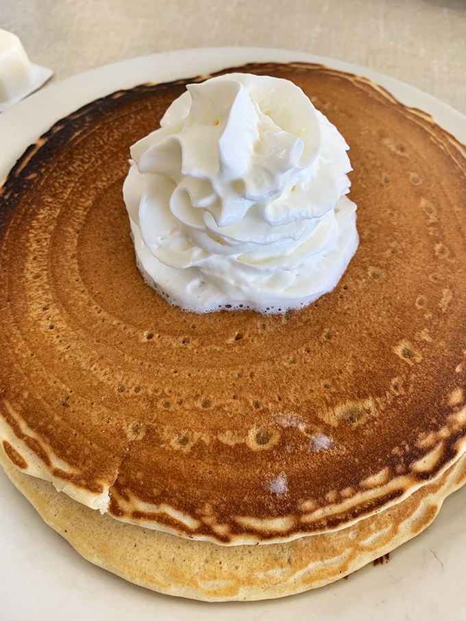 This isn't just a pancake; it's a fluffy golden canvas topped with a cloud of whipped cream that melts into every warm, buttery crevice.