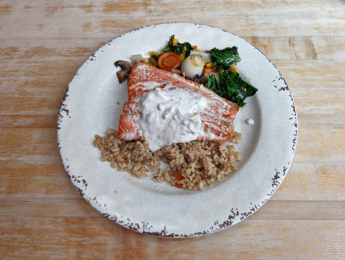 Perfectly seared salmon rests atop a bed of nutty grains, surrounded by seasonal vegetables and topped with a sauce that whispers, "Take another bite."