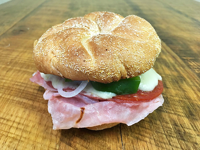 A pretzel roll cradles ham and cheese like they're precious cargo, while crisp vegetables add color commentary to this sandwich story.
