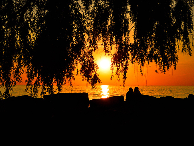 Nature's own light show at the water's edge. Two silhouettes remind us that some moments are better shared than photographed &ndash; though I couldn't resist this one.
