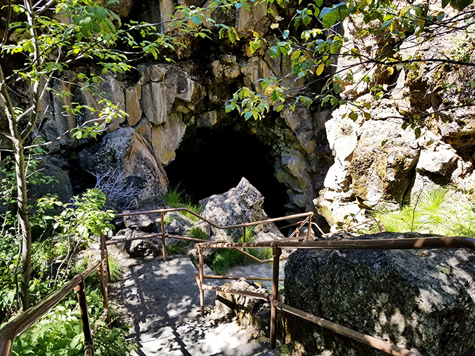 Nature's doorway beckons with primordial appeal. This rugged entrance, framed by volcanic rock and forest greenery, marks the threshold between everyday Oregon and its underground wonders.