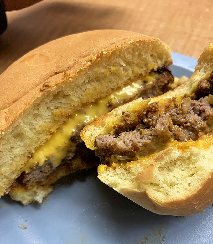The cheeseburger cross-section reveals the truth: perfectly melted American cheese embracing a hand-formed patty. Poetry between buns, no sonnet required.