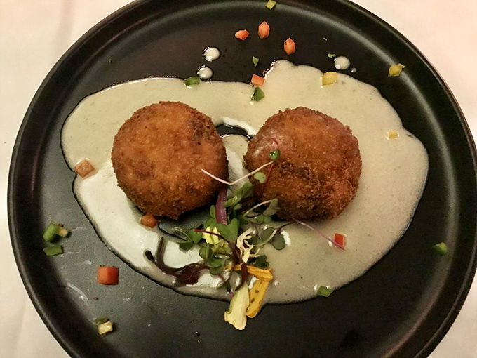 Golden crab cakes that look like they just won the lottery, sitting pretty on their elegant presentation plate.