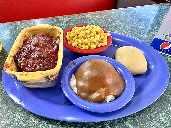 Meatloaf, mashed potatoes smothered in gravy, corn, and a roll&mdash;the Mount Rushmore of comfort food carved onto a single blue plate.