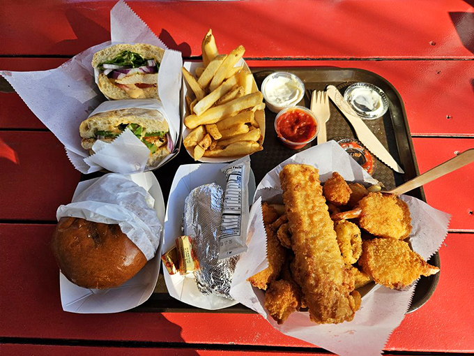 A seafood summit where crispy fish, tender sandwich, and golden fries negotiate peace terms on a red picnic table. Diplomacy never tasted so good.