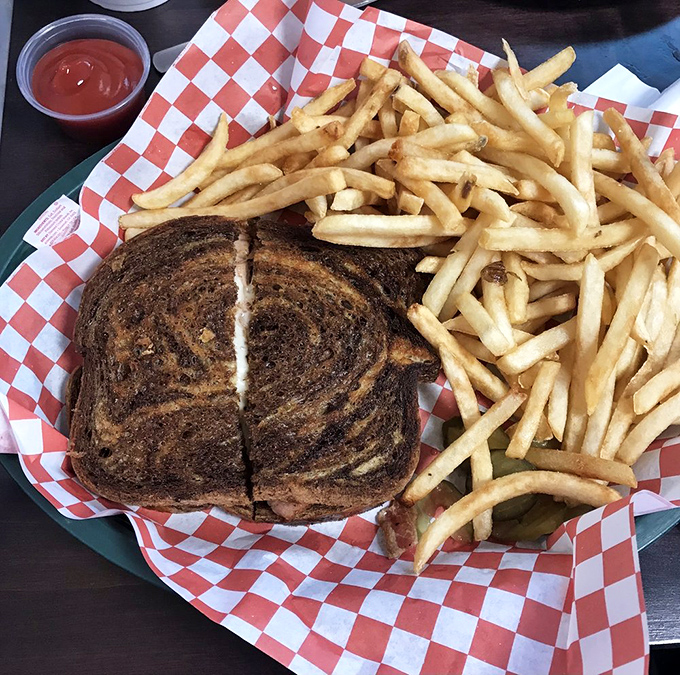 Golden fries surround a perfectly grilled sandwich like loyal subjects around their monarch. The red-checkered paper adds that classic diner touch.