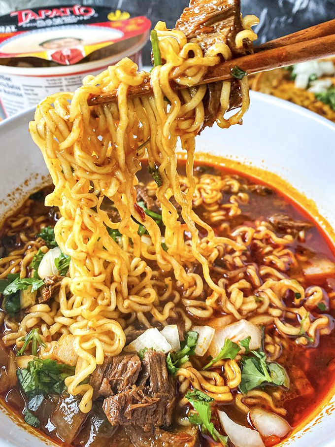 These noodles aren't just swimming in broth&mdash;they're performing synchronized flavor dives with tender beef in a spicy pool that demands your full attention.
