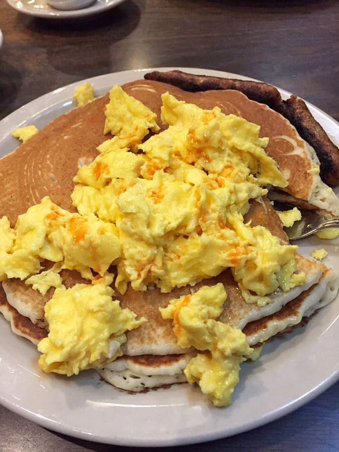Breakfast architecture at its finest: fluffy pancakes supporting a golden scramble, with bacon standing guard like delicious sentinels of flavor.