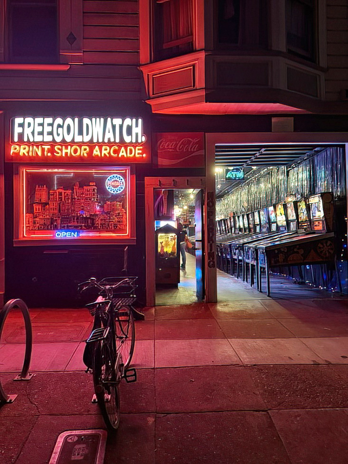 The neon sign glows with promise against the Victorian architecture. Print shop by day, arcade wonderland by night.