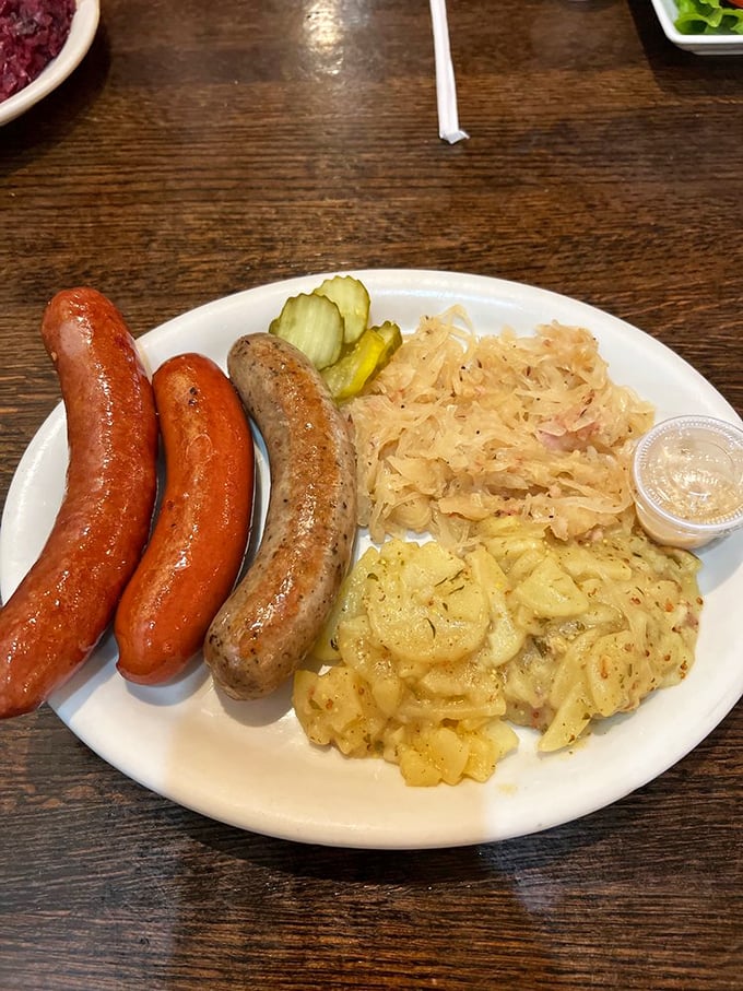 A sausage trio that would make any Bavarian proud, nestled alongside tangy sauerkraut and German potato salad &ndash; comfort food with a passport.