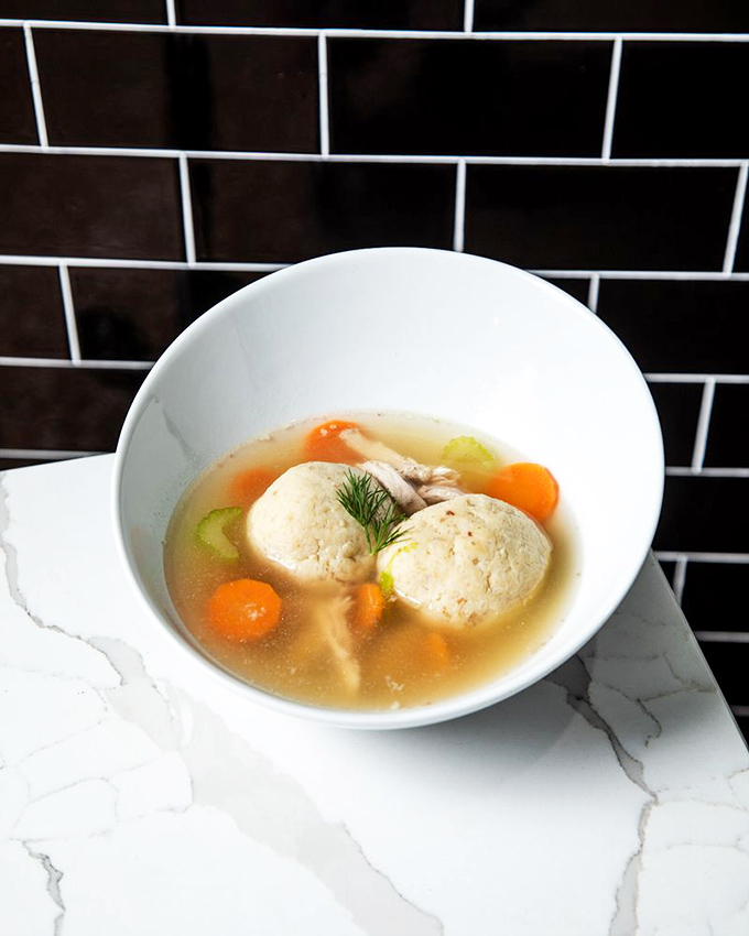 Two perfect matzo balls floating in golden broth like tiny edible planets in a universe of comfort. This soup doesn't cure colds; it cures existential crises.
